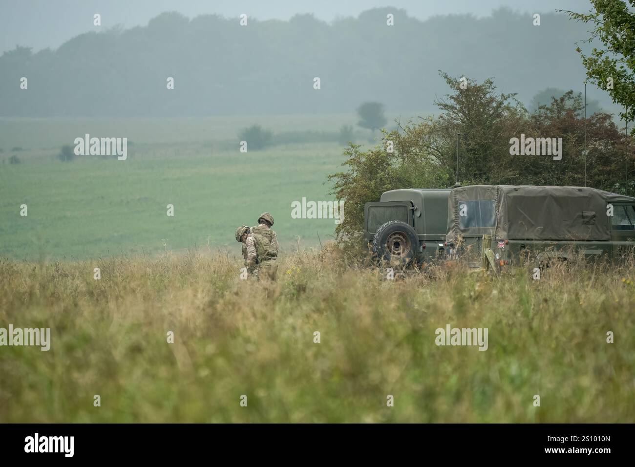 British army soldier prepares a field radio aerial mast, near two Land ...