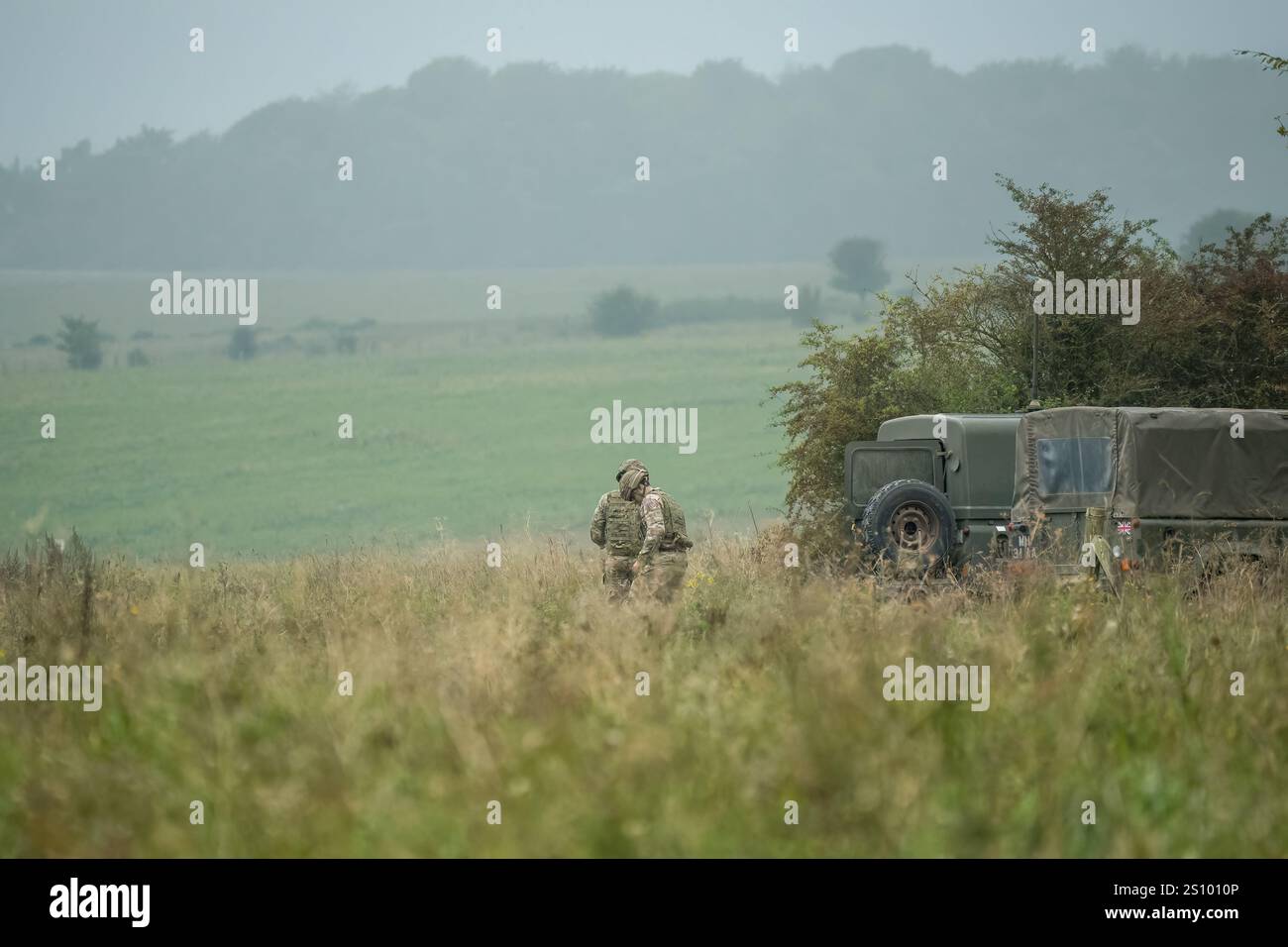 British army soldier prepares a field radio aerial mast, near two Land ...