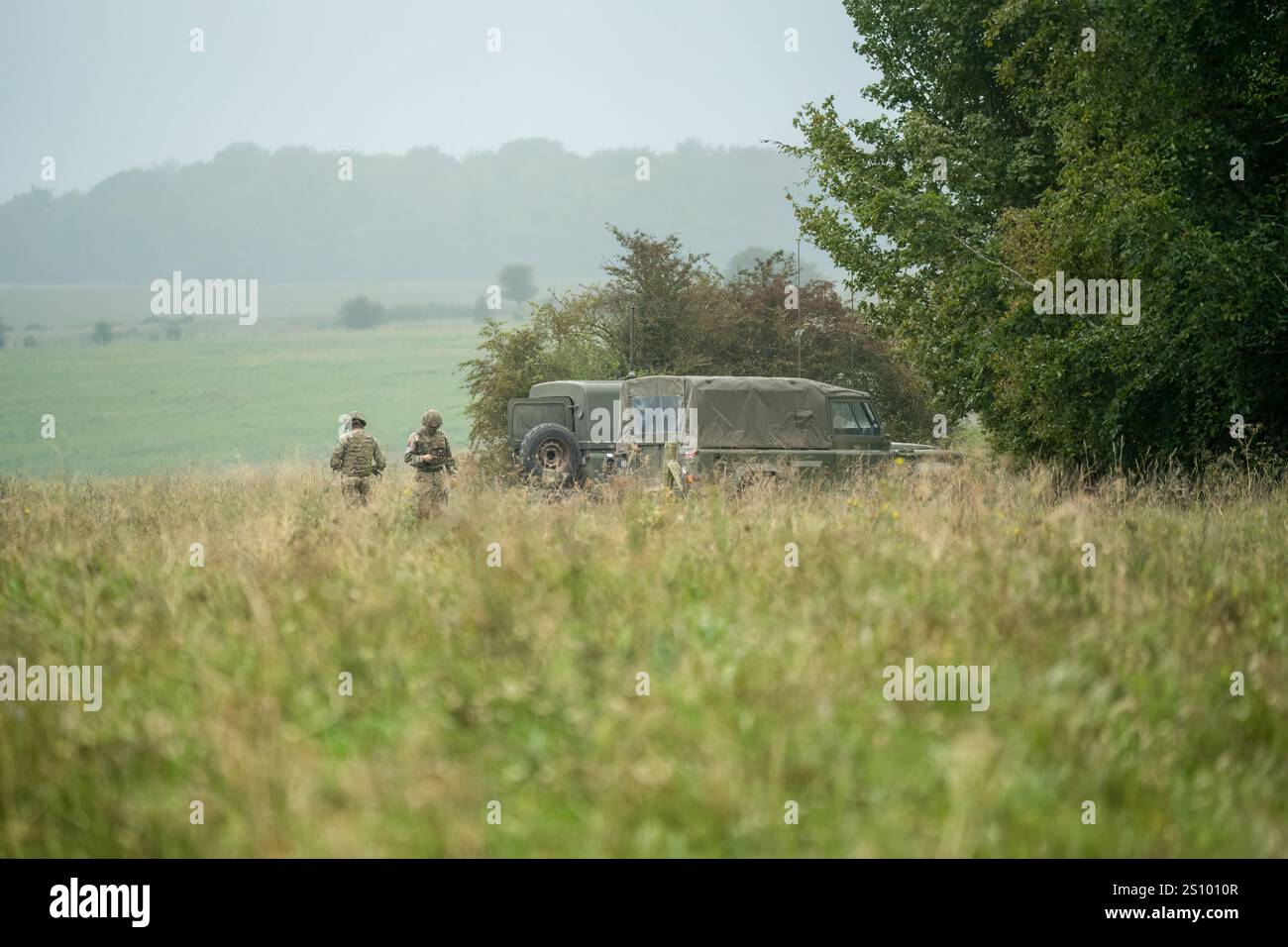 British army soldier prepares a field radio aerial mast, near two Land ...
