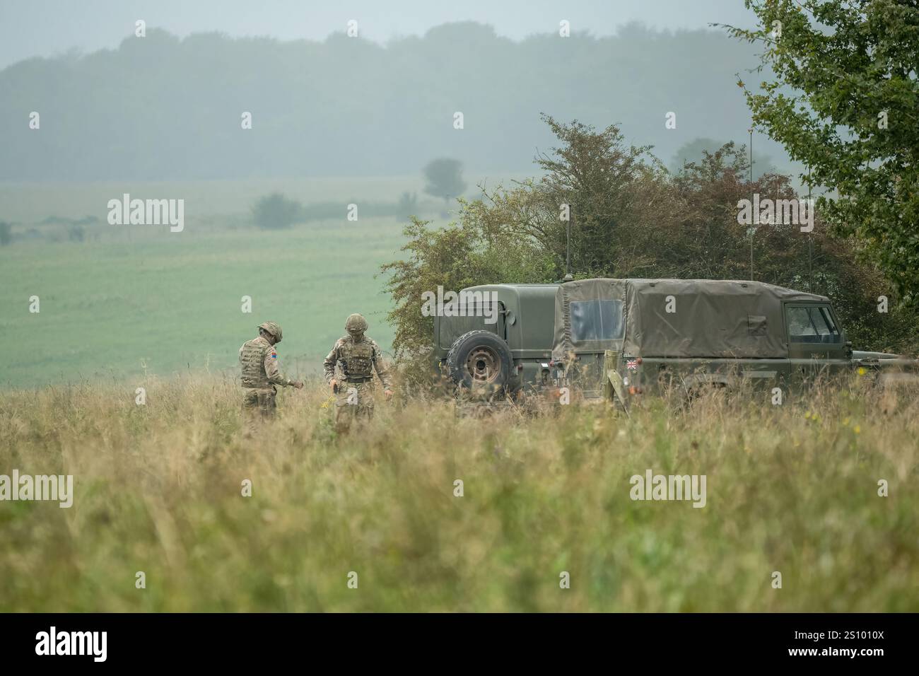 British army soldier prepares a field radio aerial mast, near two Land ...