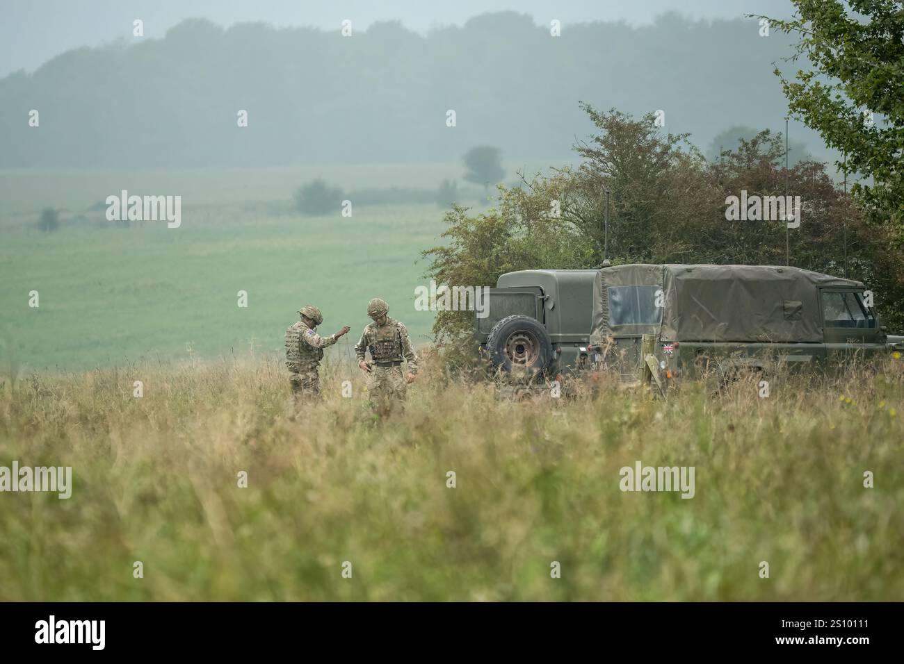 British army soldier prepares a field radio aerial mast, near two Land ...