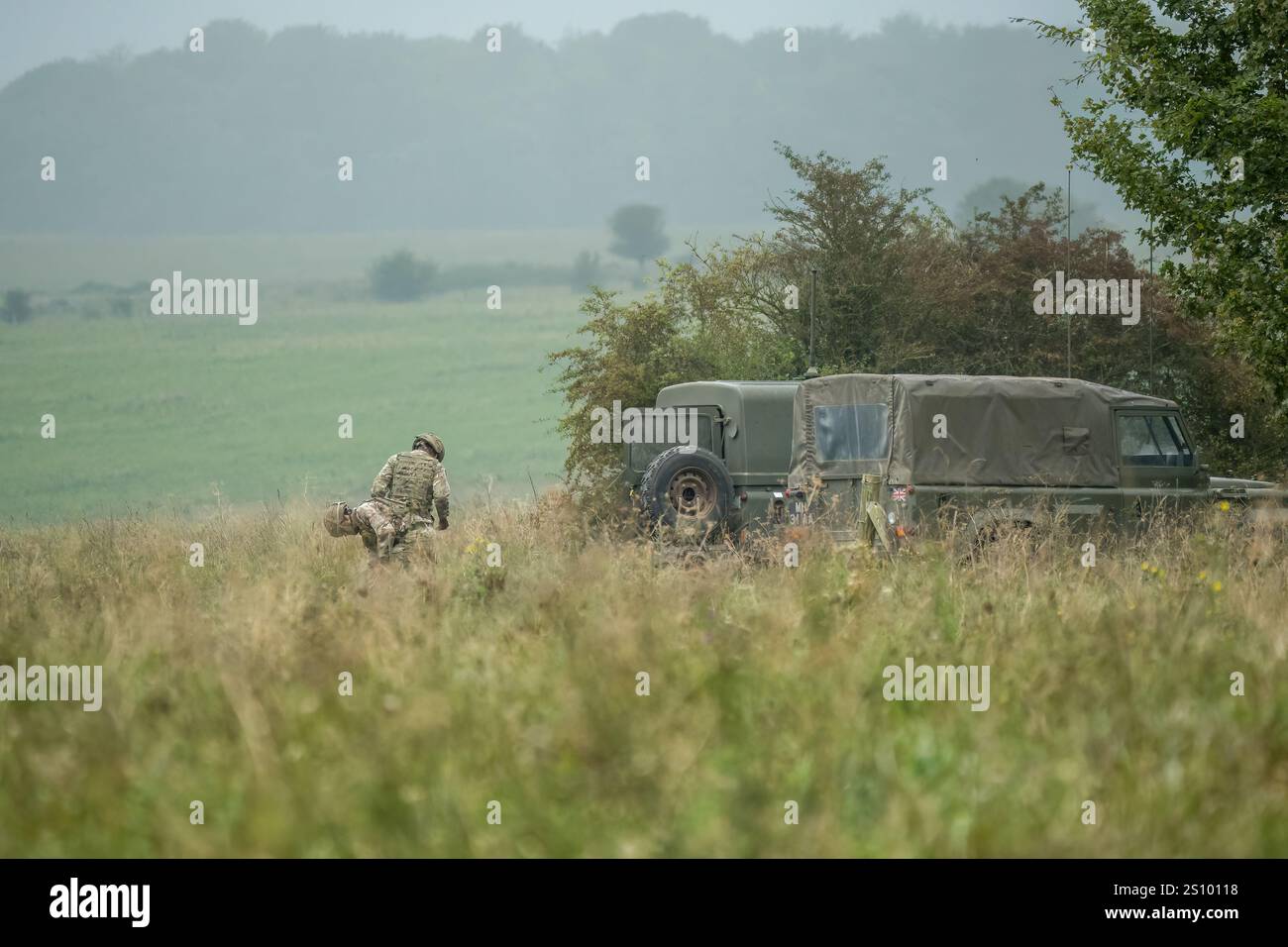 British army soldier prepares a field radio aerial mast, near two Land ...