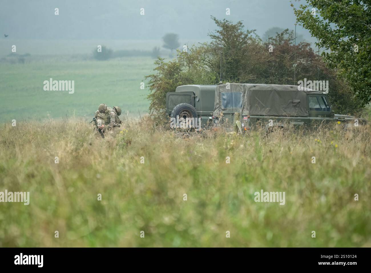 British army soldier prepares a field radio aerial mast, near two Land ...