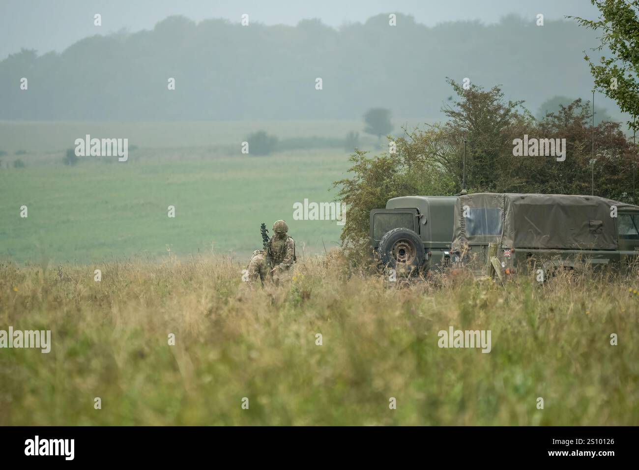 British army soldier prepares a field radio aerial mast, near two Land ...