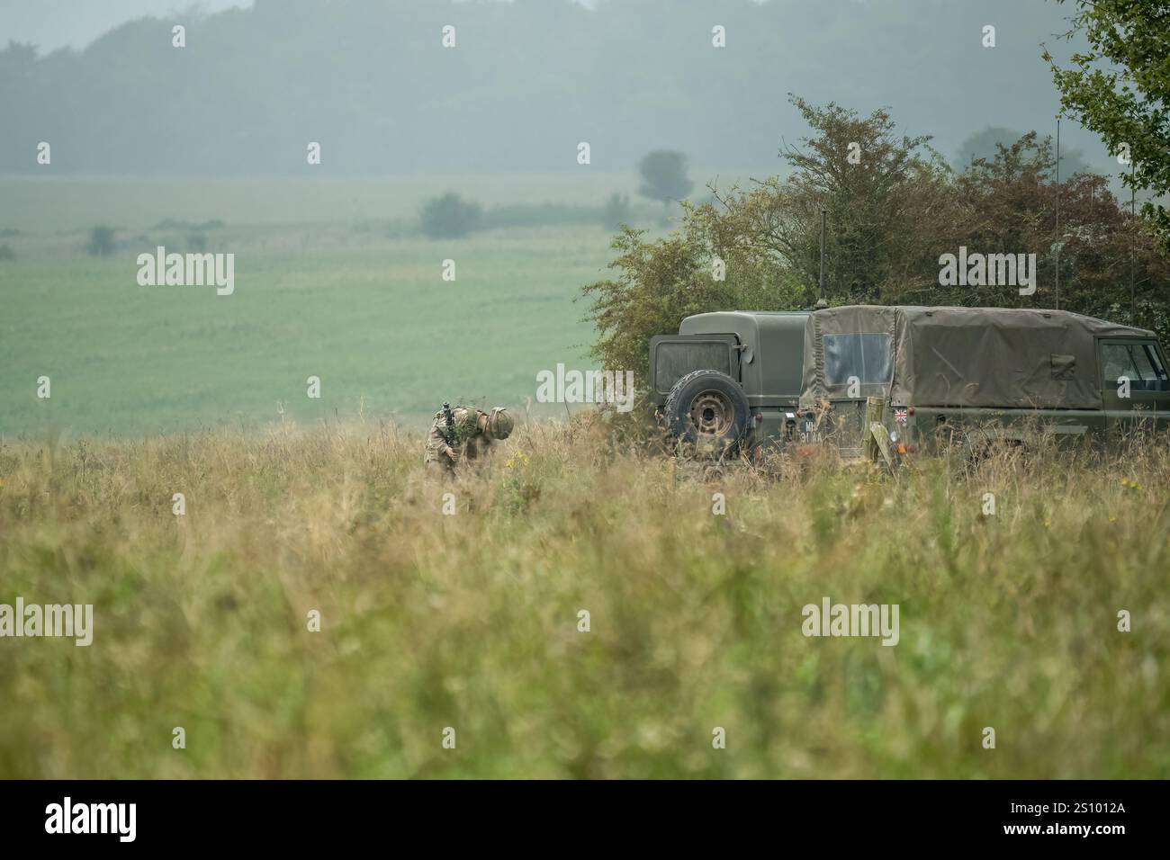 British army soldier prepares a field radio aerial mast, near two Land ...