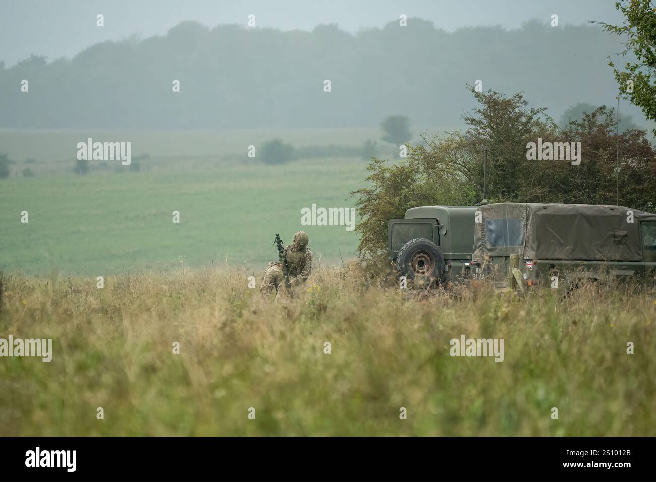 British army soldier prepares a field radio aerial mast, near two Land ...