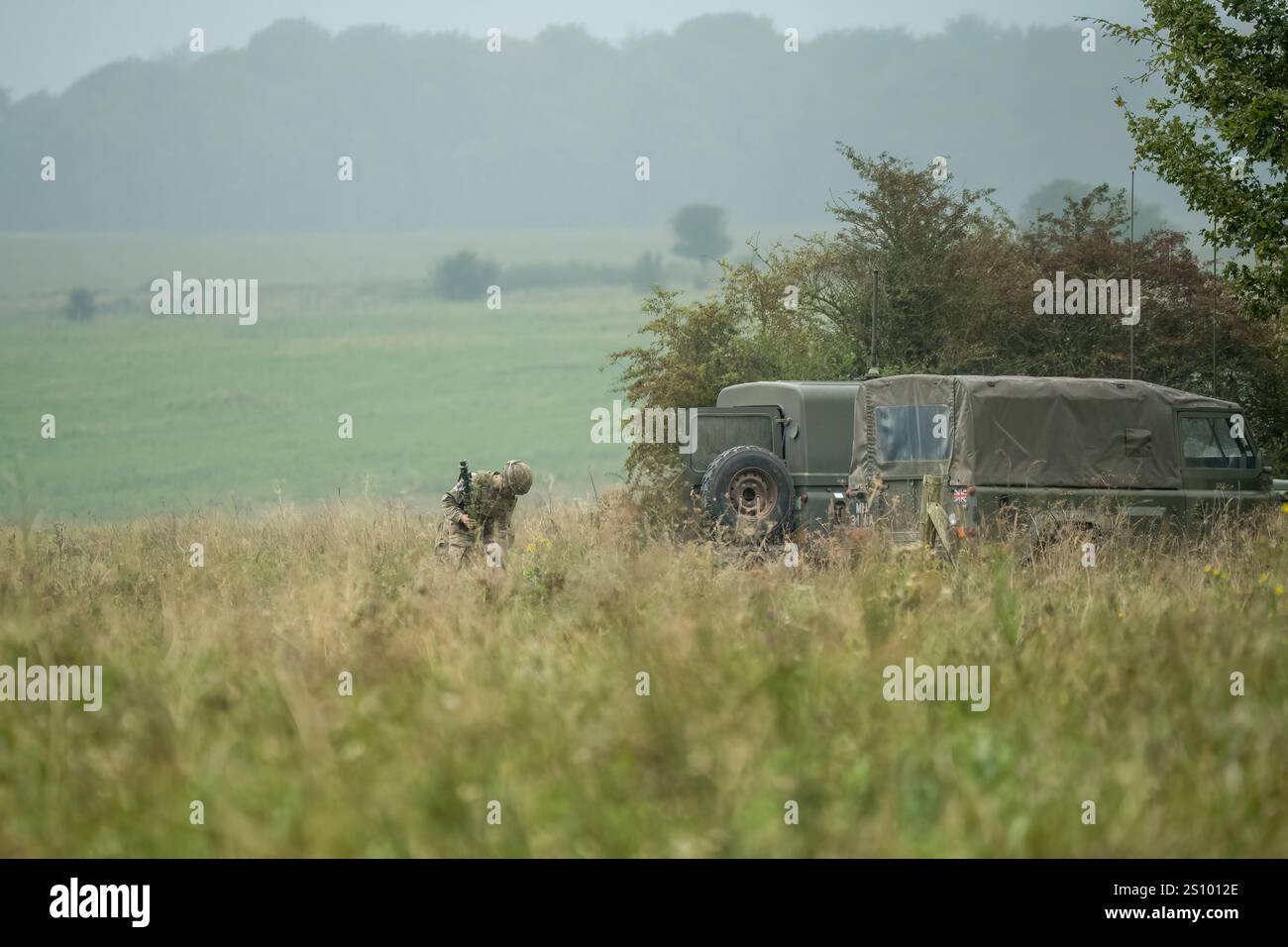British army soldier prepares a field radio aerial mast, near two Land ...