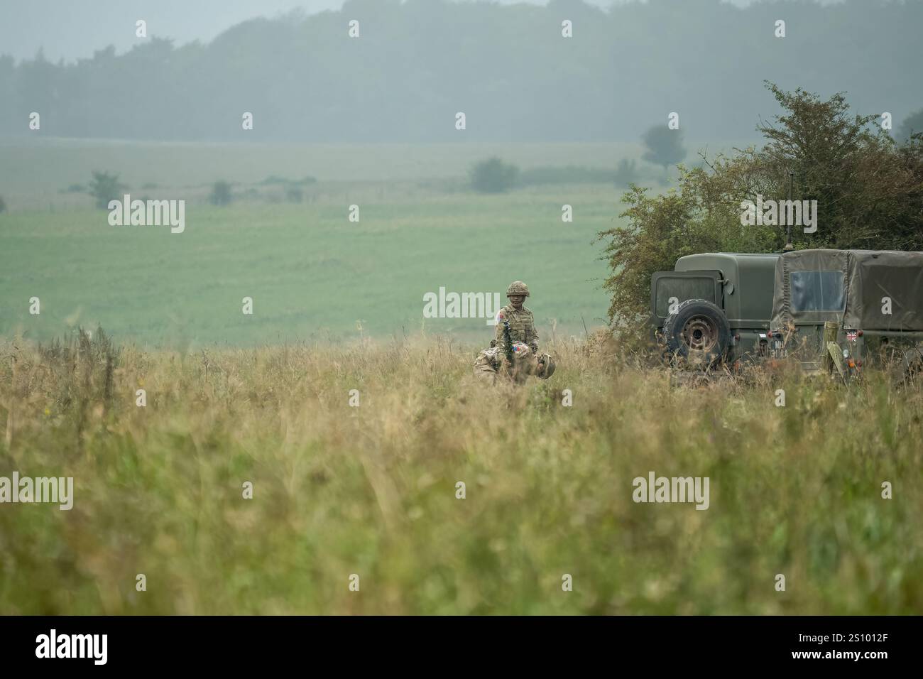 British army soldier prepares a field radio aerial mast, near two Land ...