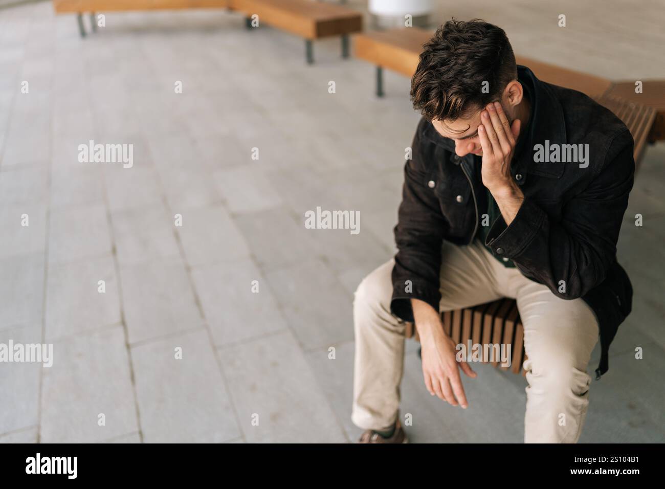 High-angle view of stressed young man sitting on bench, holding head in ...