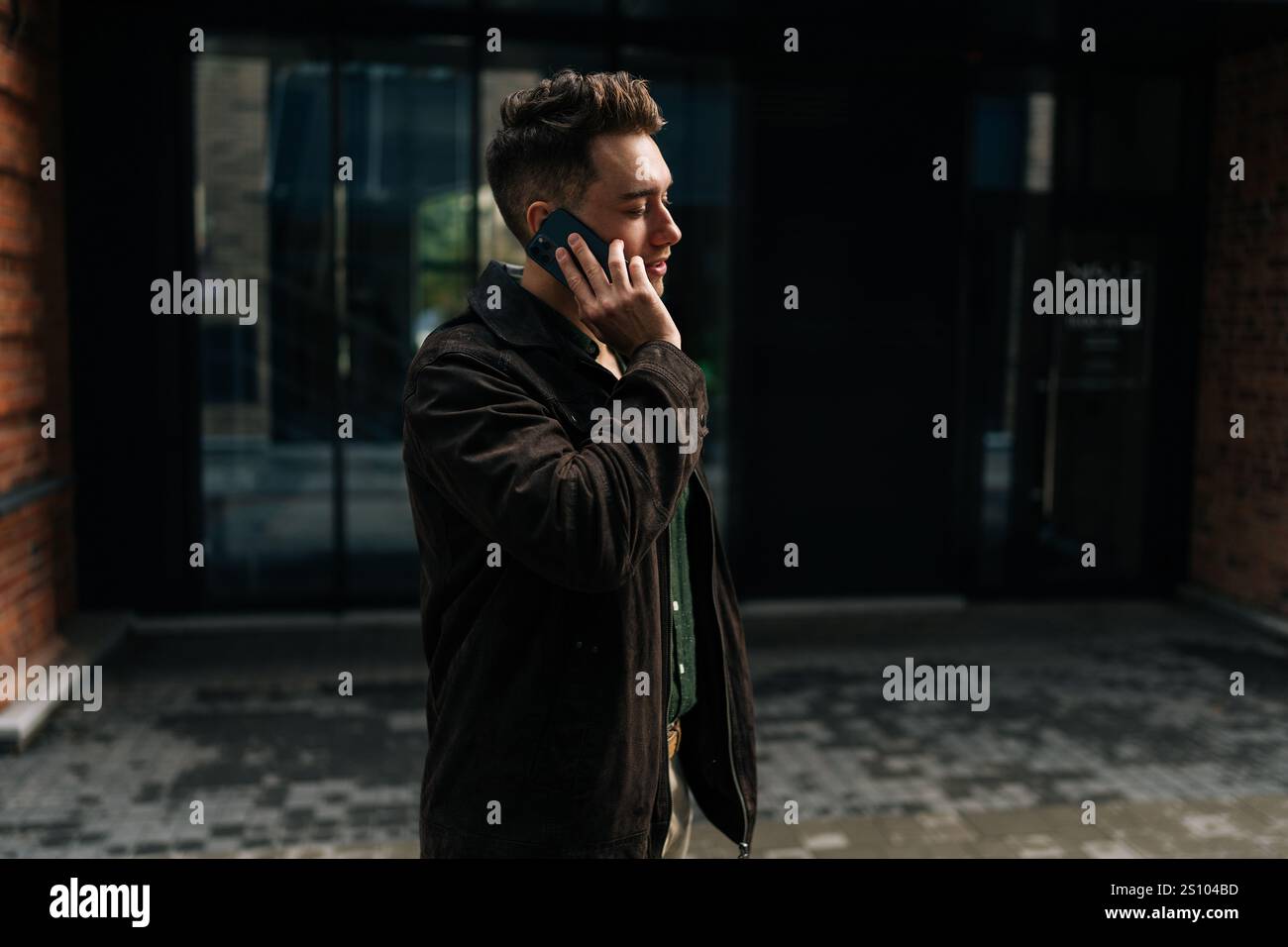 Side view of stylish young man making phone call standing outside ...