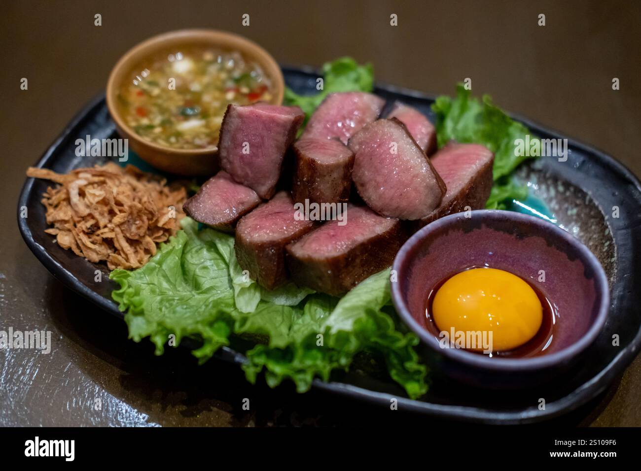 Grilled beef tongue served on plate with pickled egg yolk and sauce ...