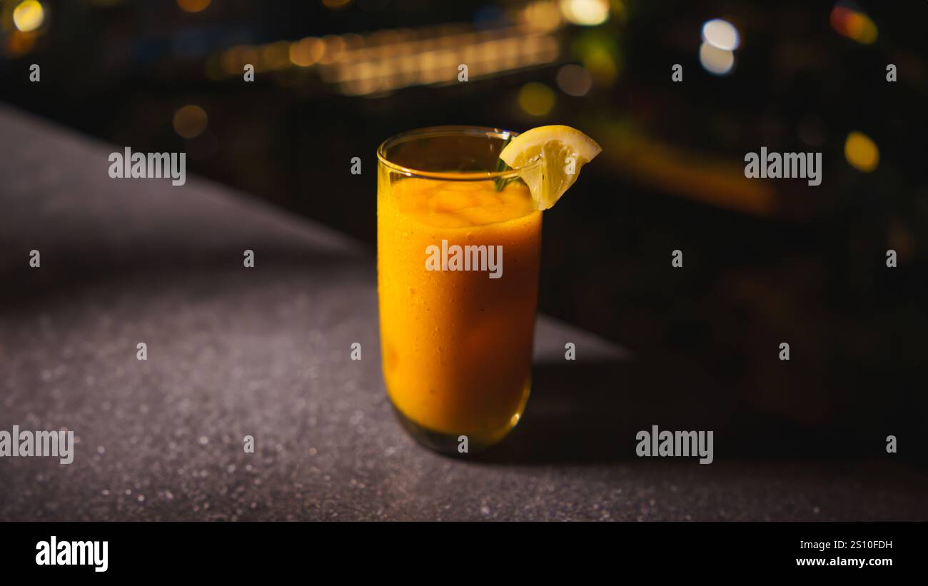 Frosty mango cocktail with lime garnish on a dark bar counter, with ...