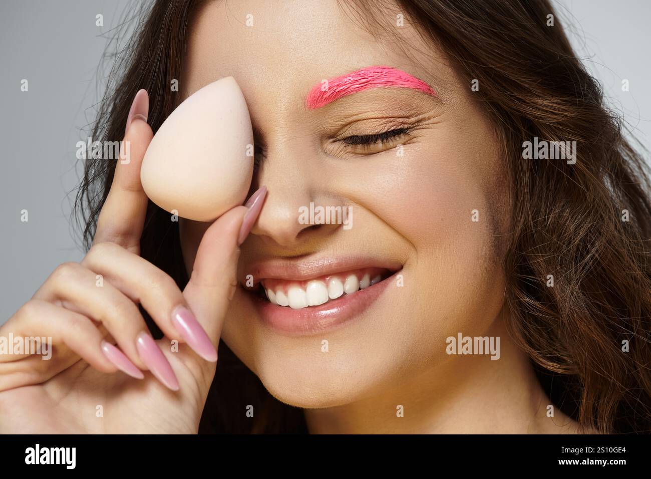 A young woman highlights her striking pink eyebrows while playfully ...