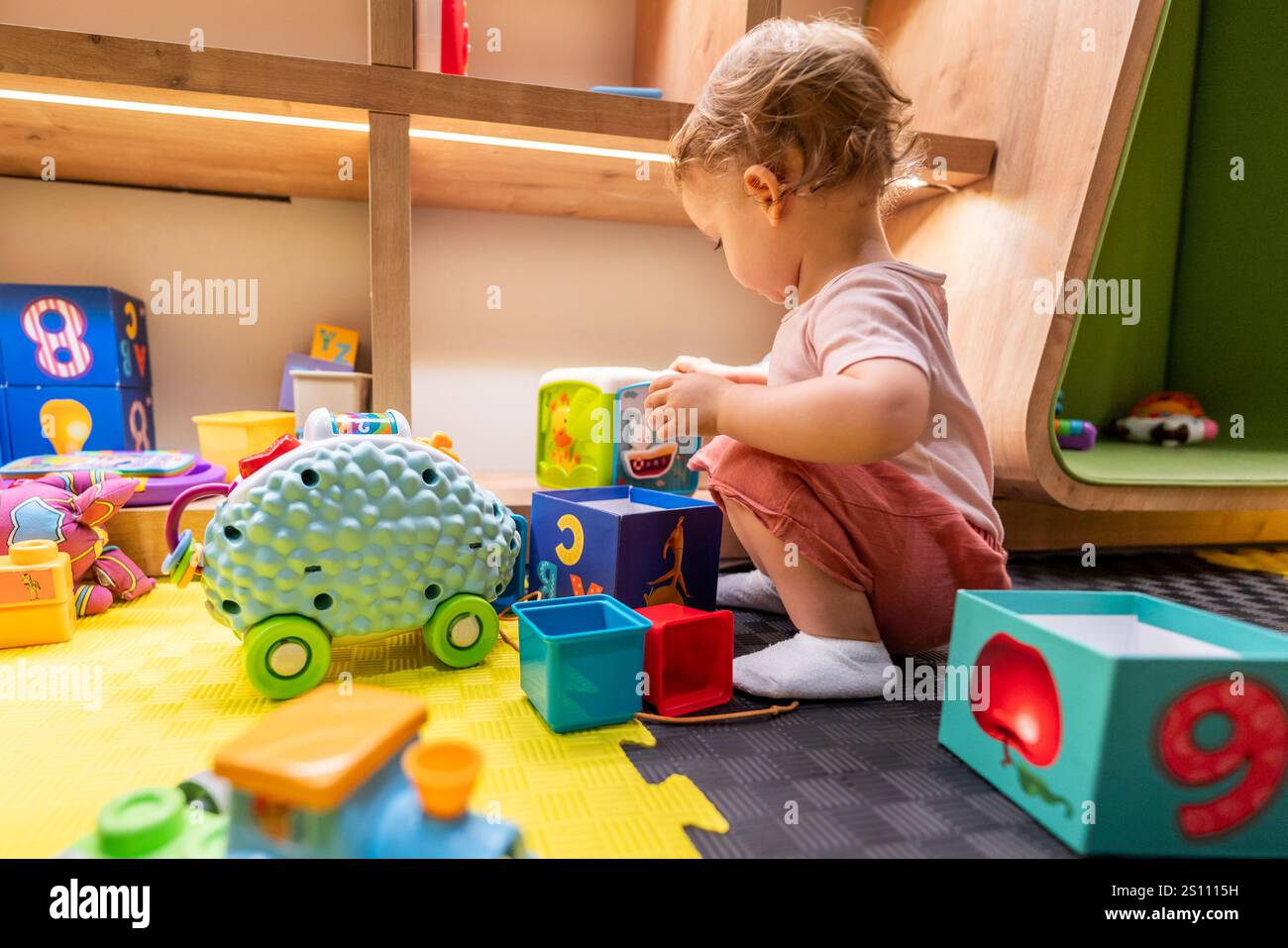 Young child stacking blocks and exploring toys in a colorful indoor ...
