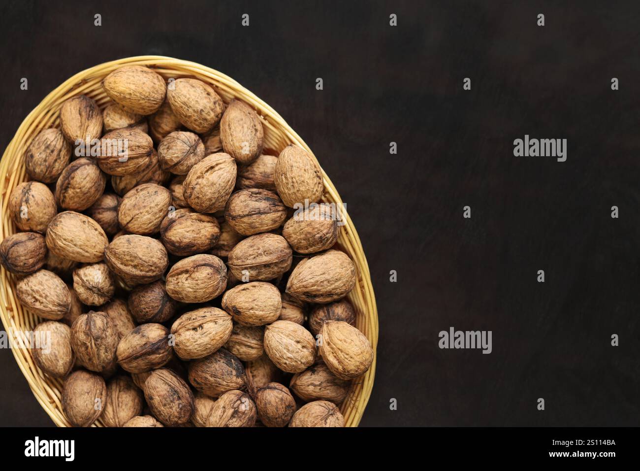 Walnuts in a wicker basket on a dark wooden background. Nuts in an oval ...