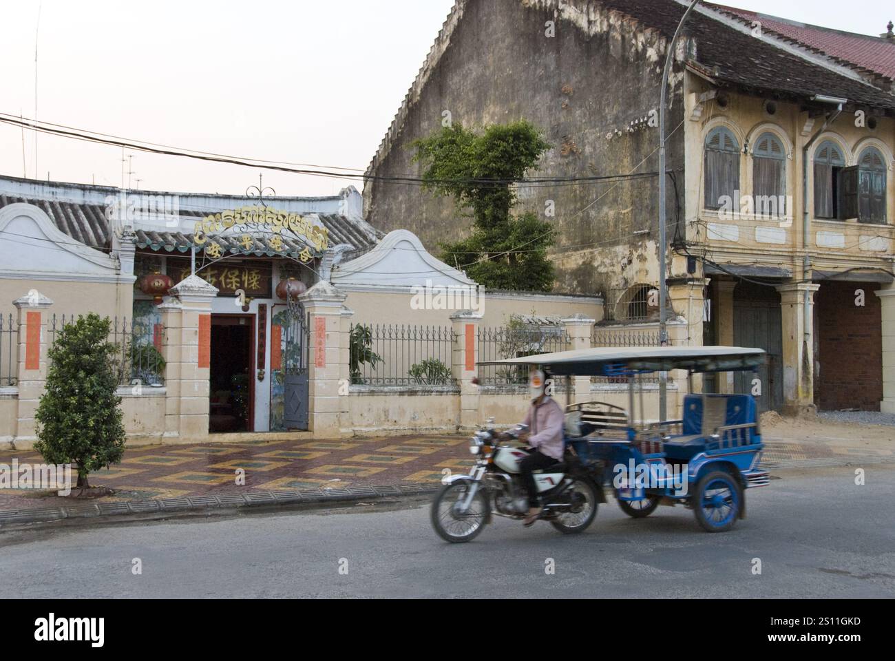 A Tuk-Tuk drives past a Chinese temple and French colonial buildings in ...