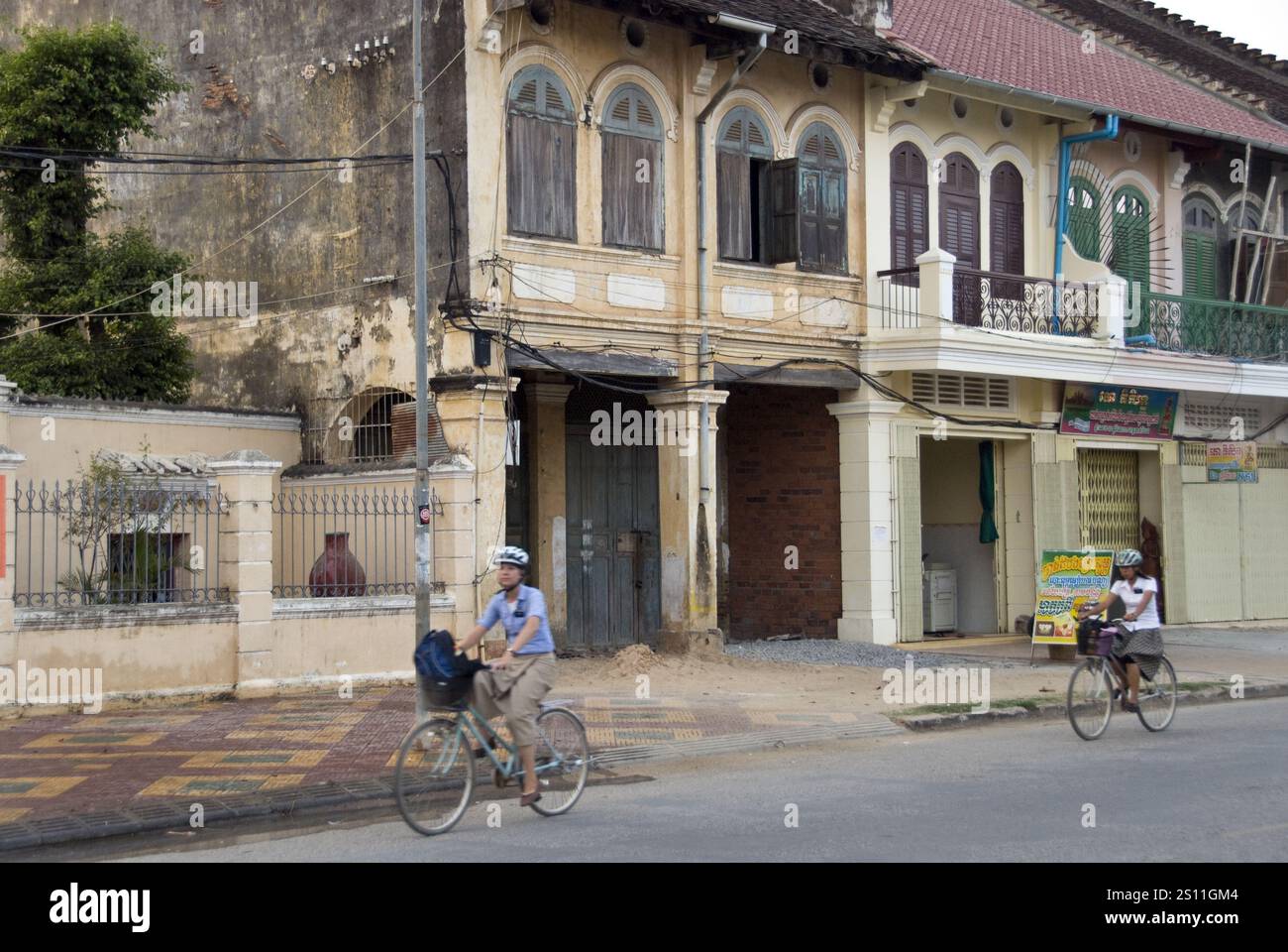 Girls ride bikes past old French Colonial buildings in Battambang, the ...