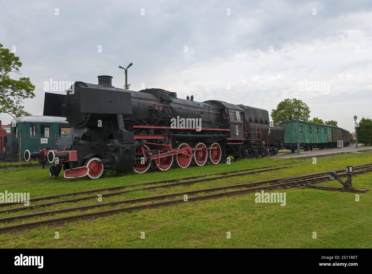 Historic steam locomotive with green wagons on a track under a cloudy ...