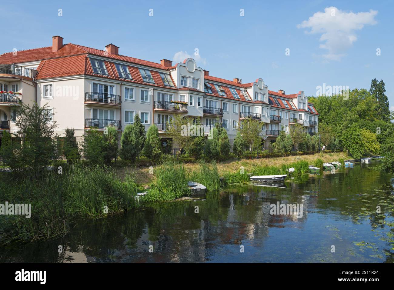 Modern residential buildings on a quiet riverbank with small boats and ...