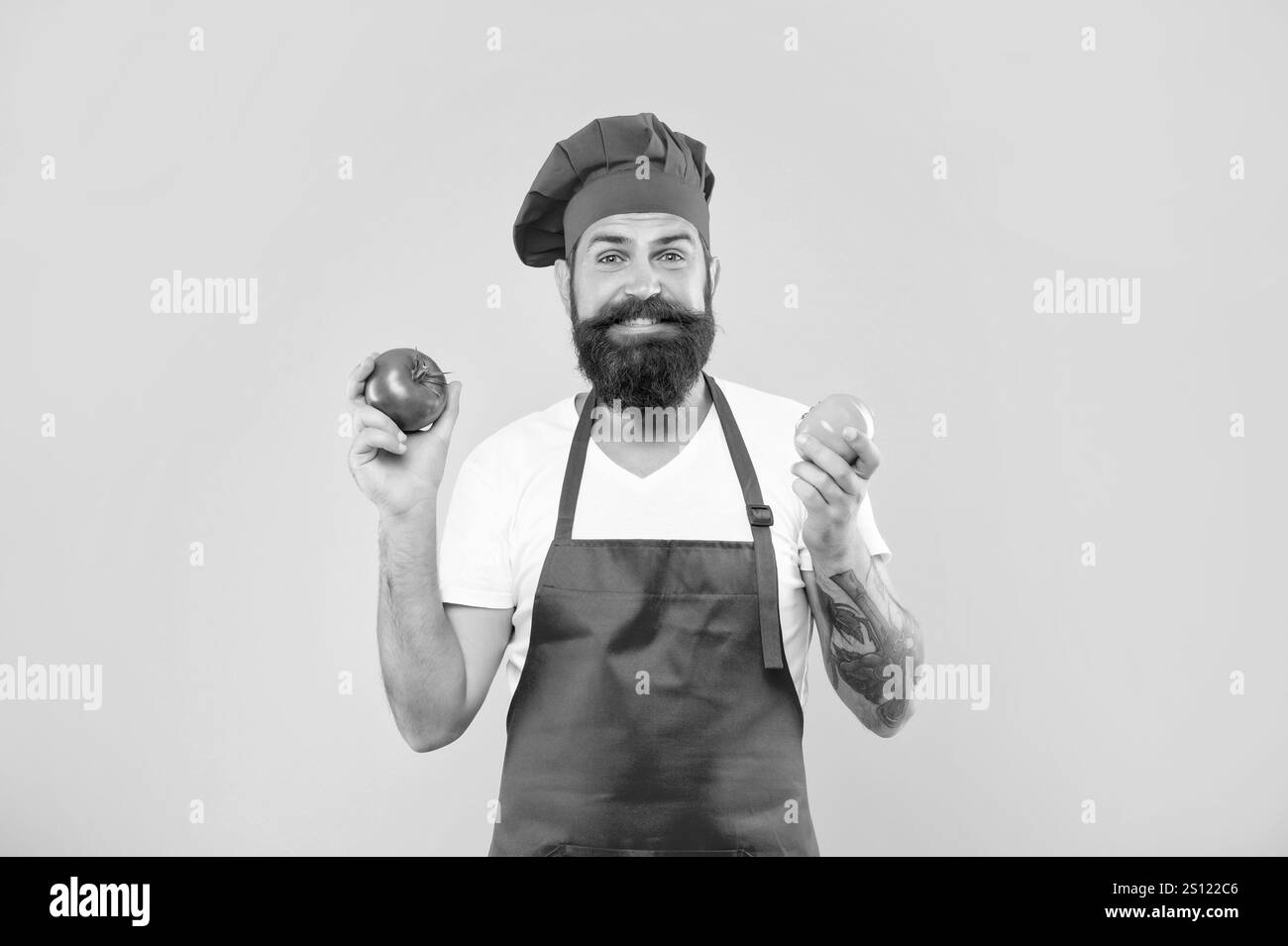 Happy man in cooking apron and toque holding red and yellow tomatoes ...