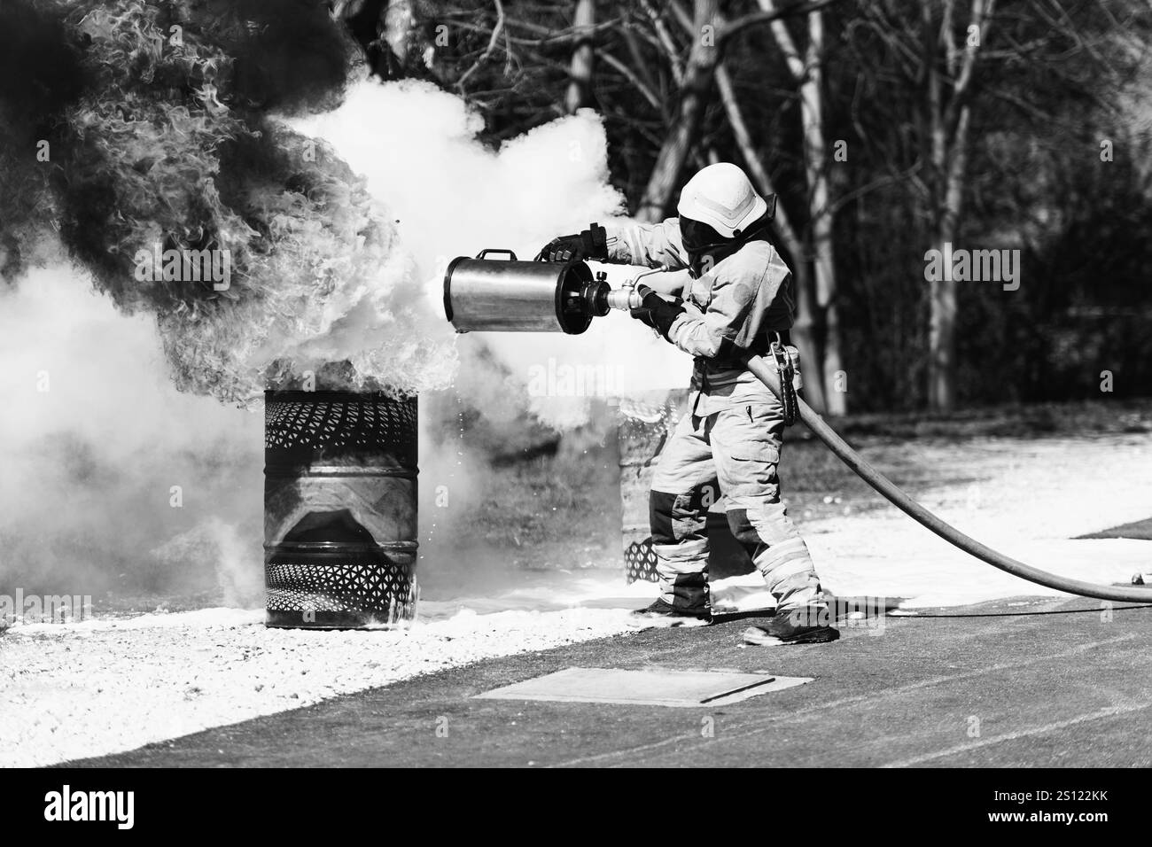 Professional firefighter battling flames on a metal oil can near road ...