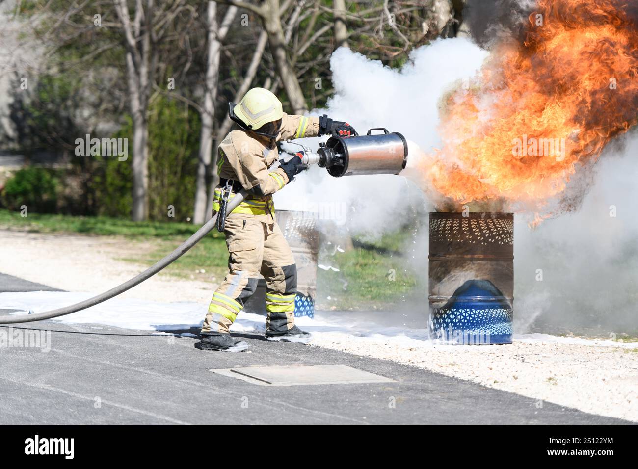 Firefighter in aged yellow uniform fighting oil can fire with foam in ...