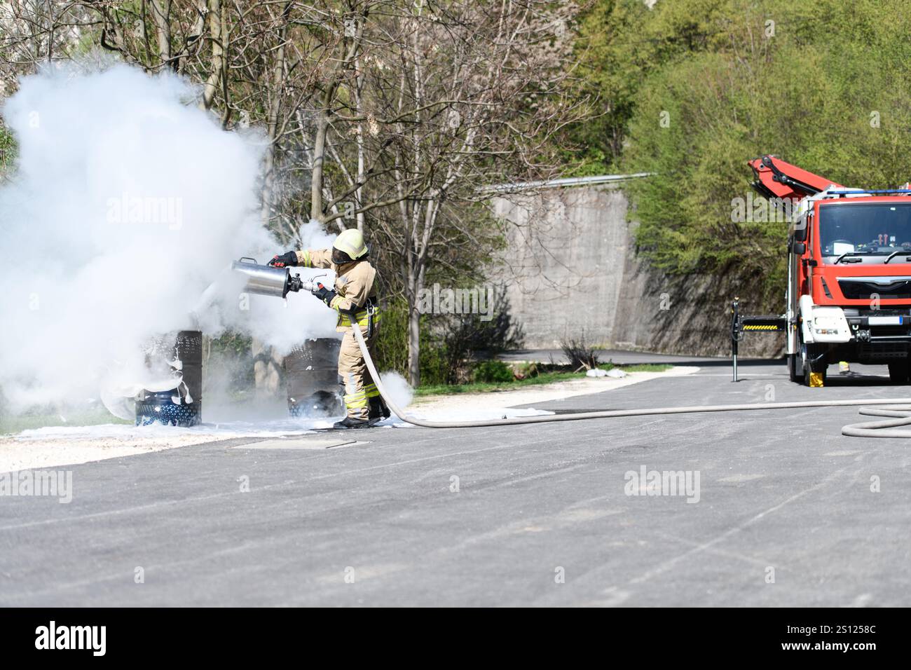 Professional firefighter battling flames on a metal oil can near road ...