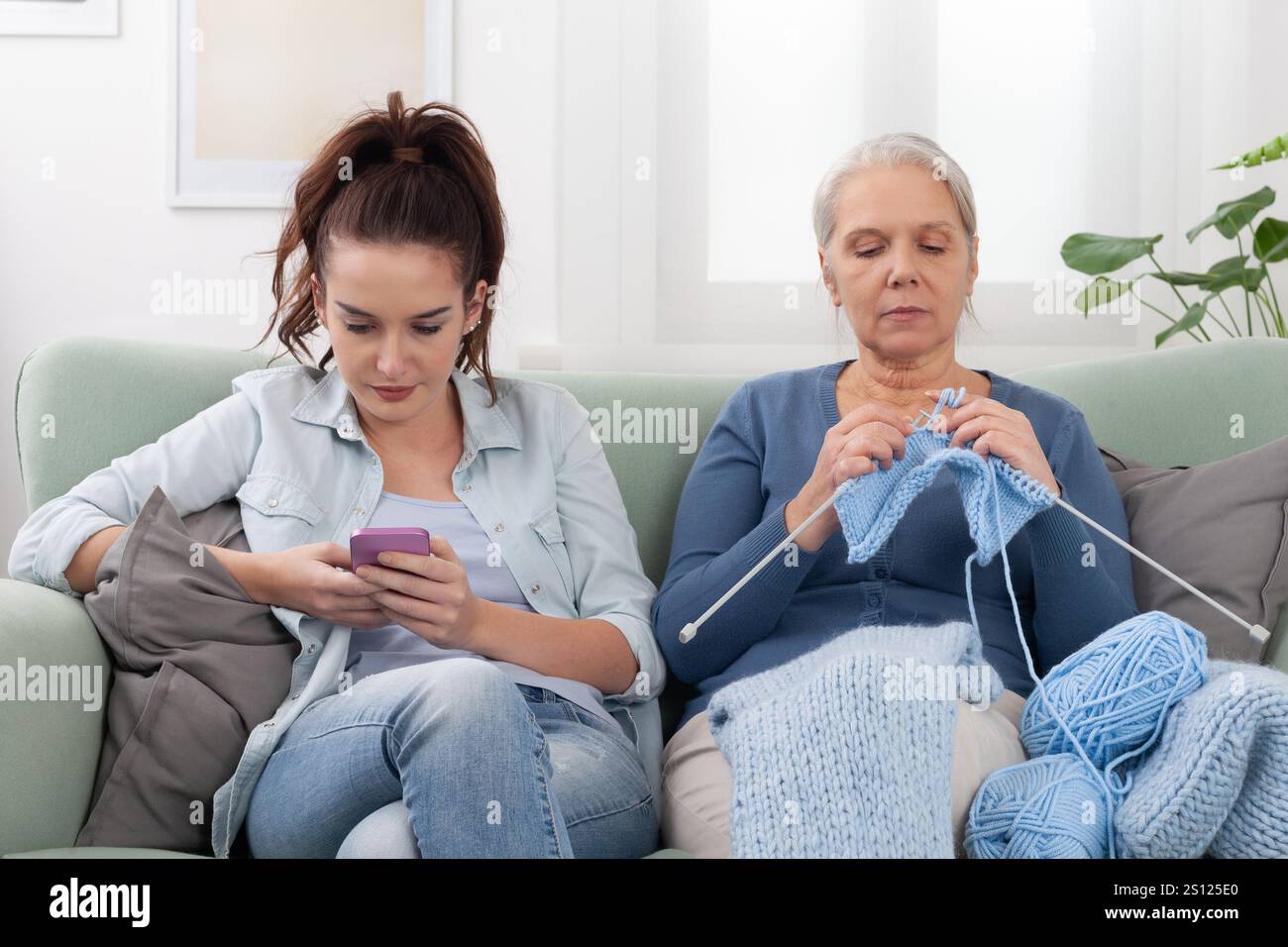 At home on the couch, a Millennials daughter uses her smartphone to ...