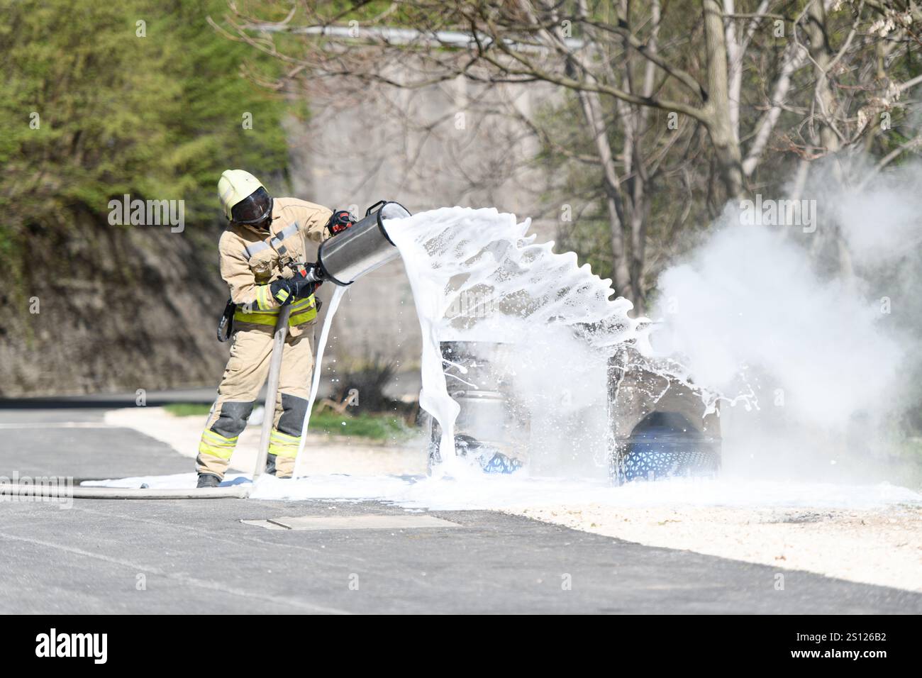Professional firefighter battling flames on a metal oil can near road ...