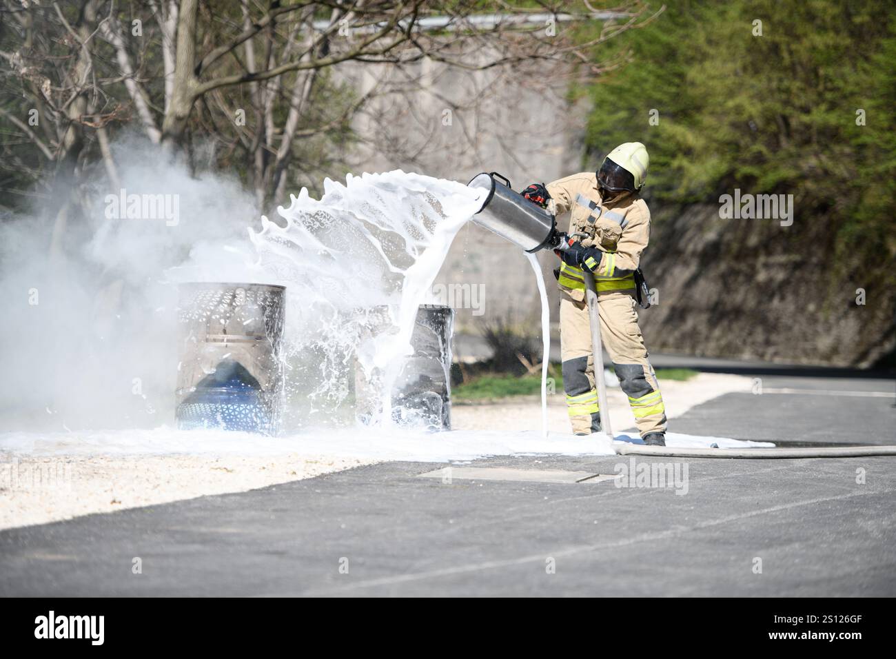 Firefighter in aged yellow uniform fighting oil can fire with foam in ...