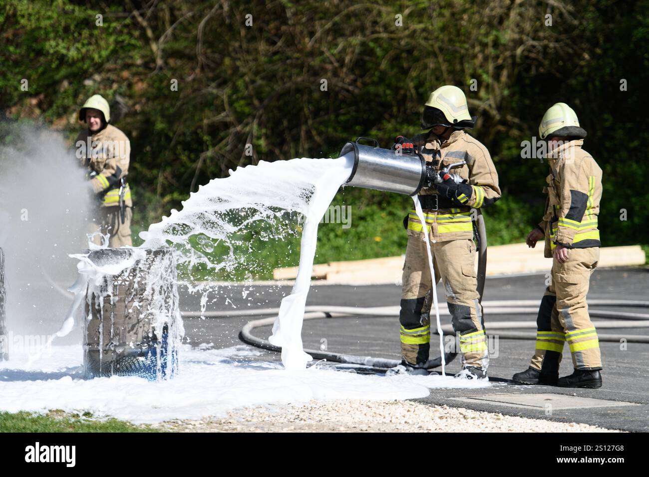 Professional firefighter battling flames on a metal oil can near road ...