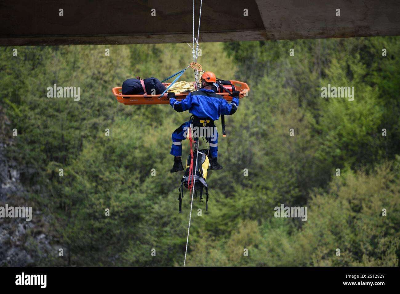 Rescuer with orange helmet and stretcher descending bridge for ...