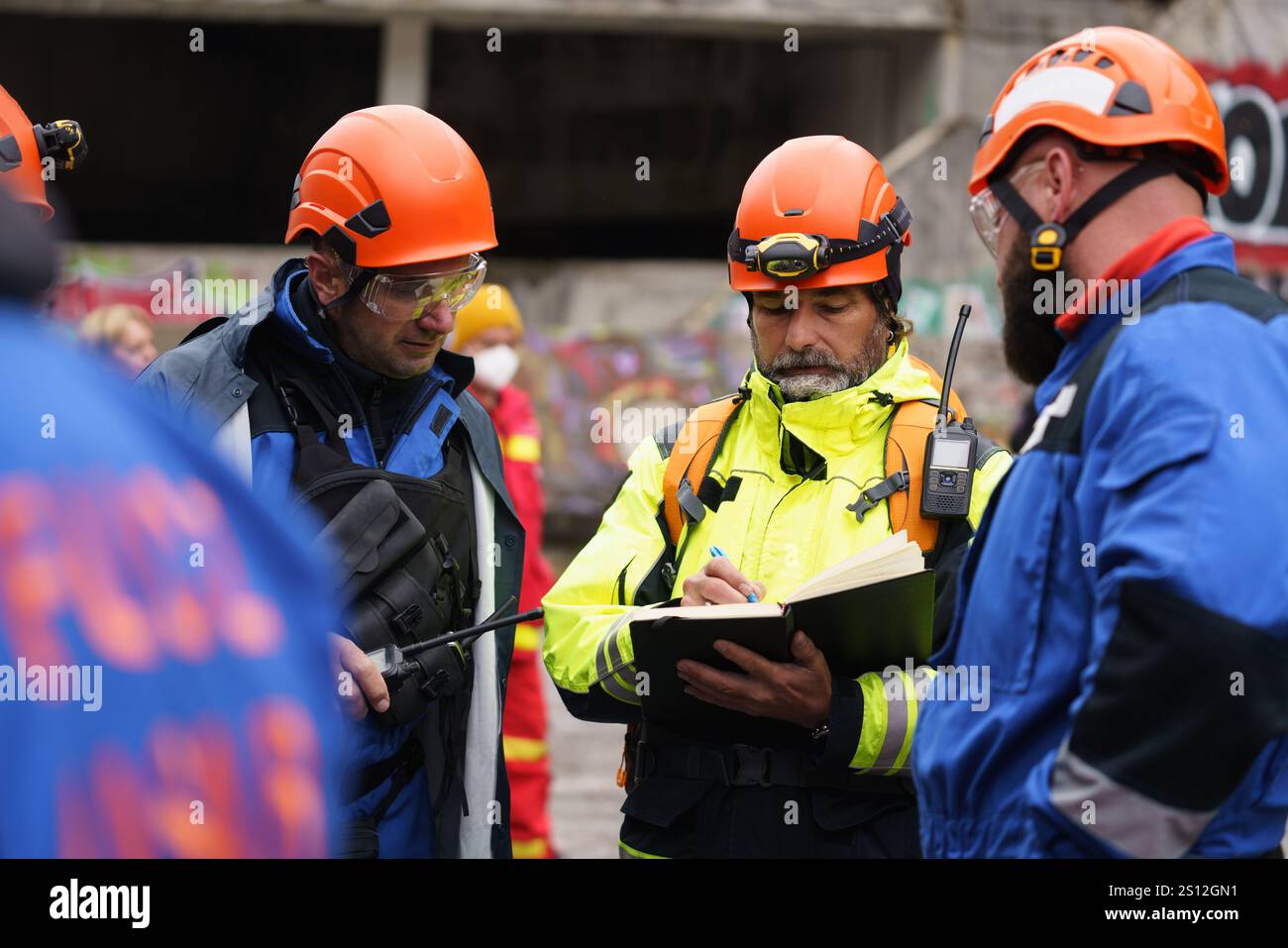 Three rescue leaders in blue uniforms and orange helmets planning next ...