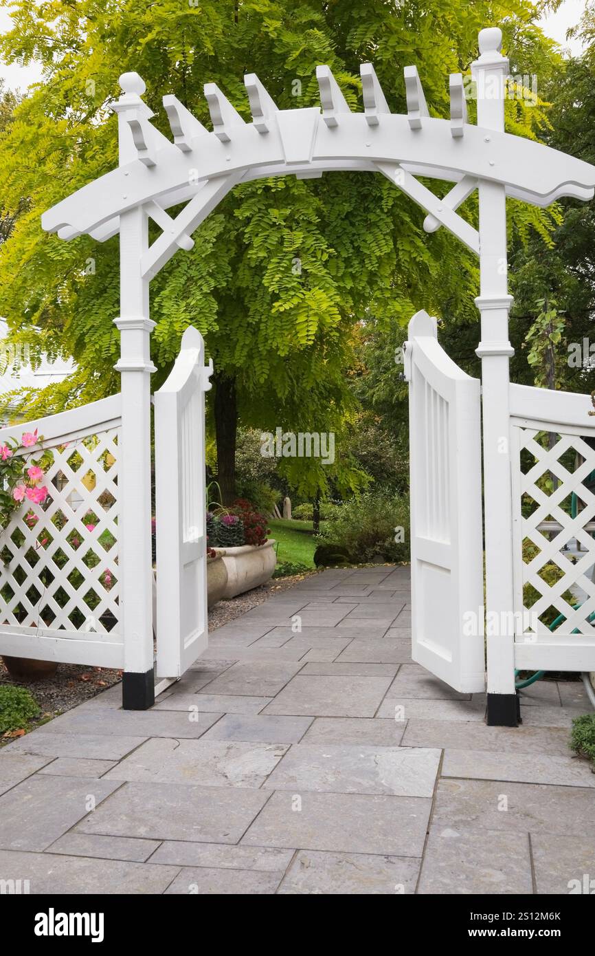 White arbour with entrance gate and lattice fence and grey flagstone ...