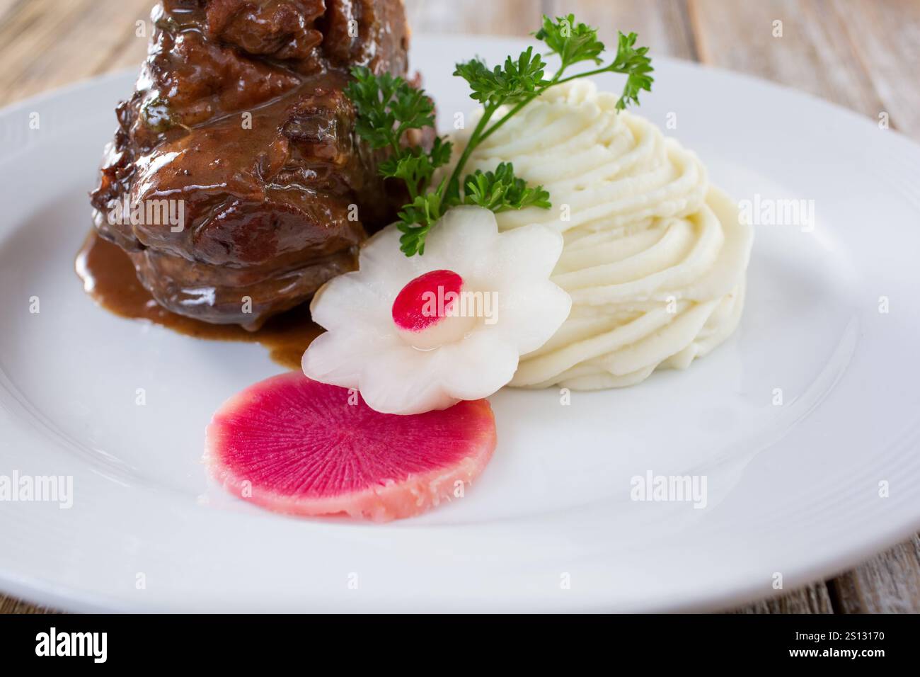 A view of a radish garnish, next to mashed potatoes and a lamb shank ...