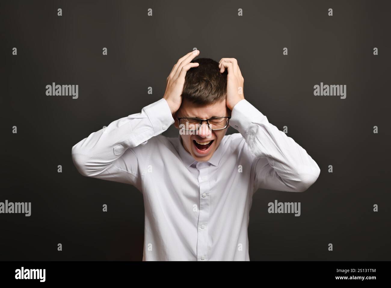 a young man, clutching his head in his hands, screams in pain and anger ...