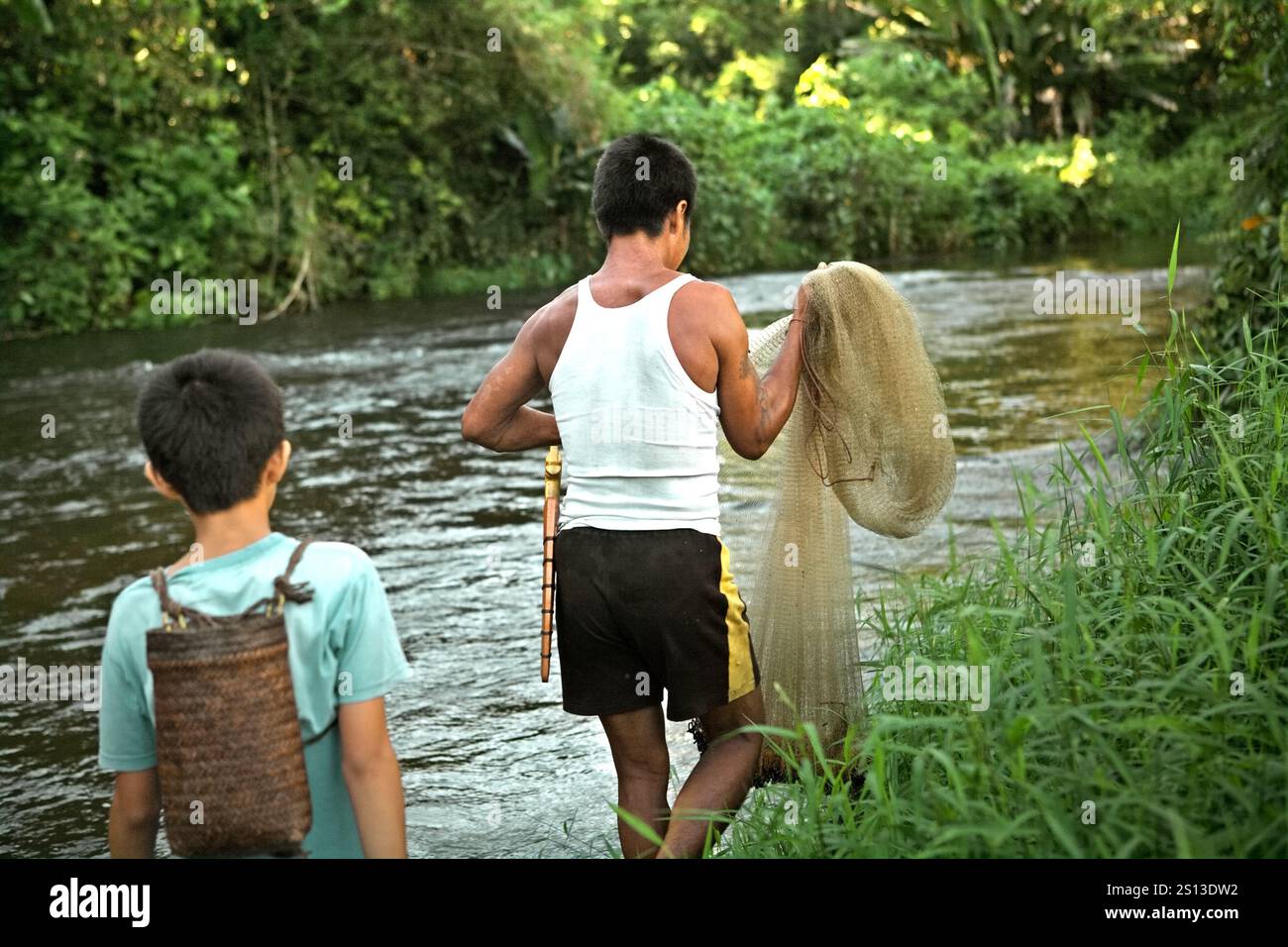 A man carrying a fishing net as he is walking on riverbank with a child in Sungai Utik, Embaloh ...