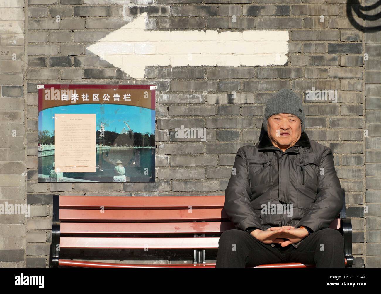 A man sits on a bench in a historical Hutong alley formed by ...