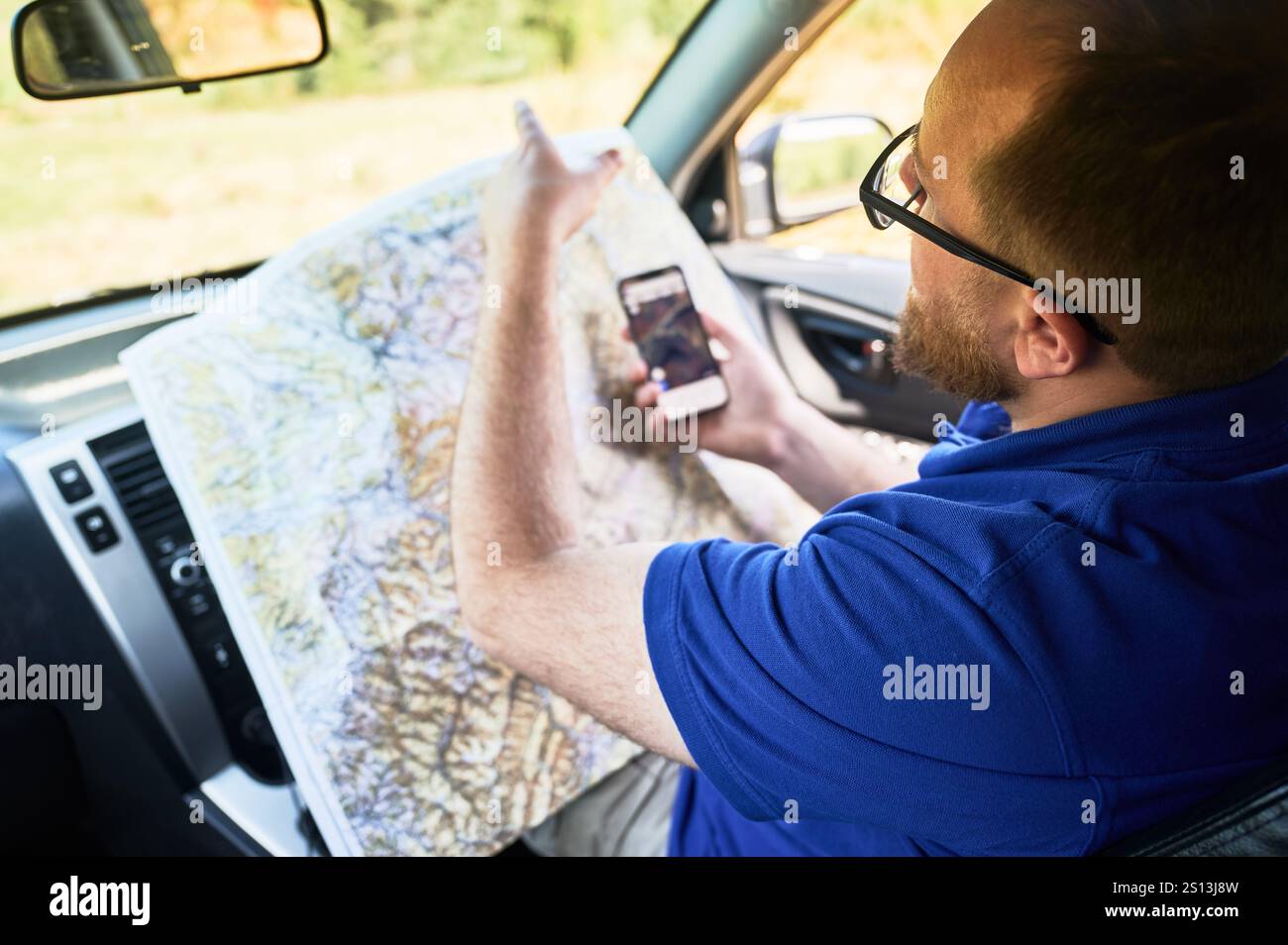 Man tourist sits in passenger seat of car, holding map and smartphone ...