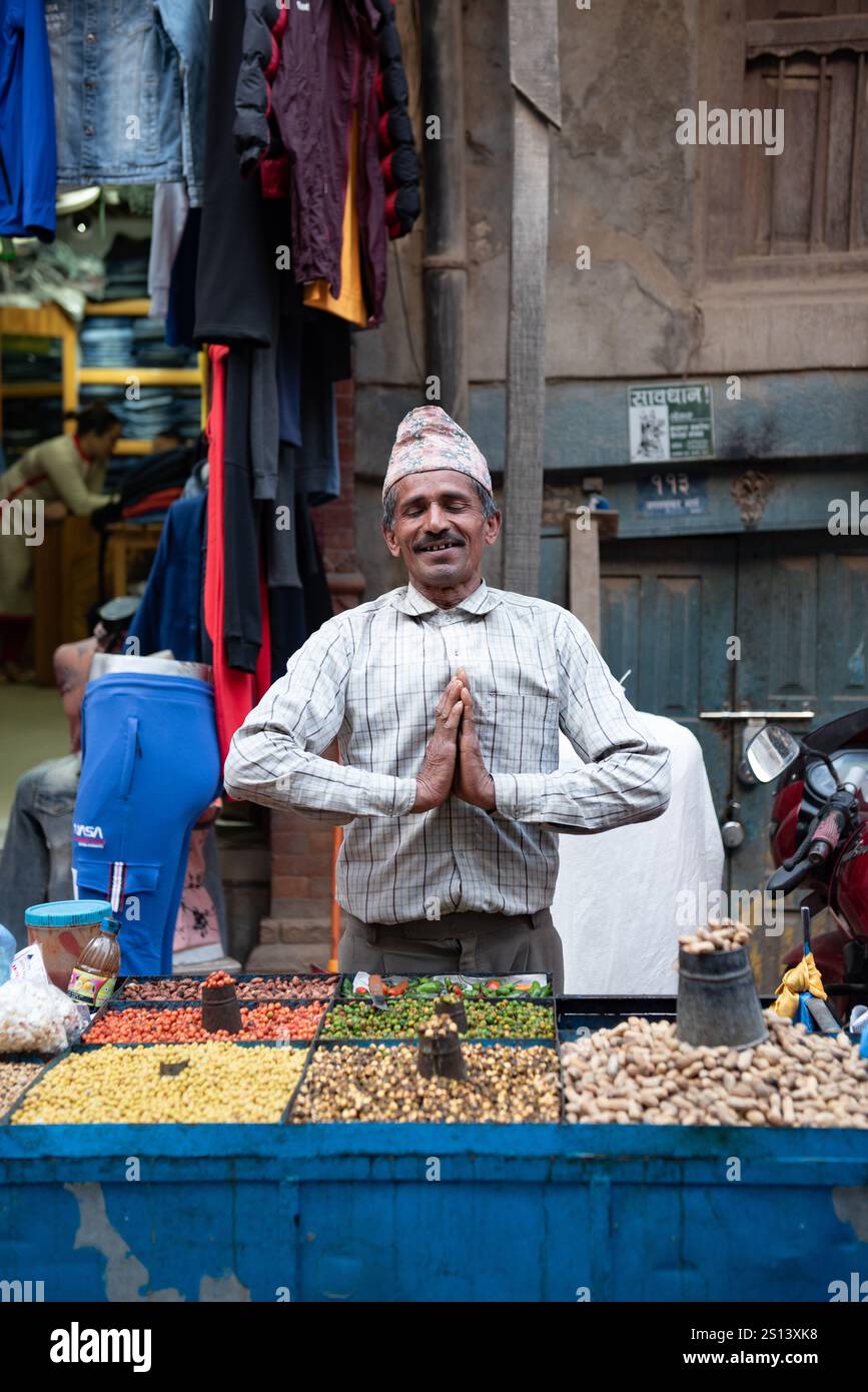 Nepali street vendor with traditional dhaka topi hat performing namaste ...