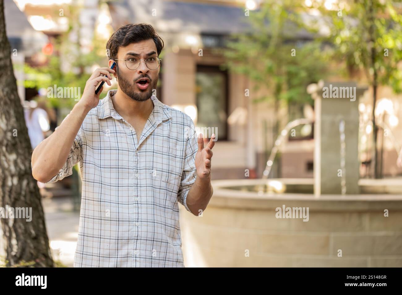 Angry mad stressed Indian young man arguing while talking on smartphone ...