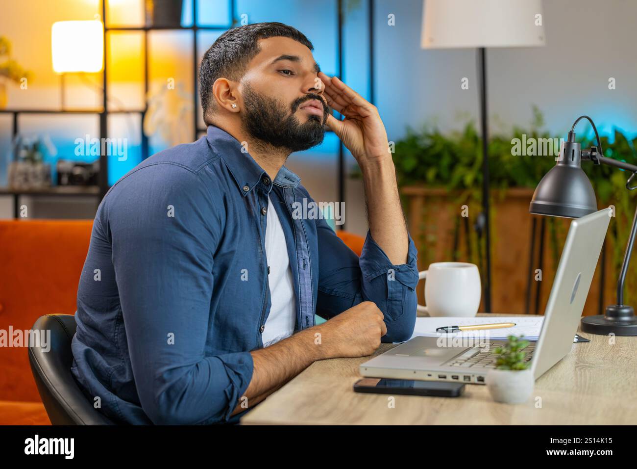 Bored sleepy young Indian bearded man working on laptop computer ...