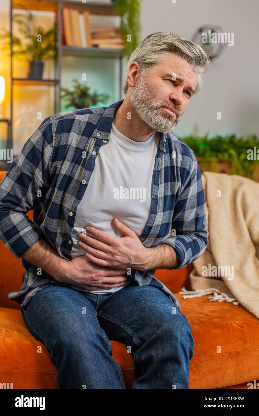Senior man sitting on couch feeling sudden strong abdominal stomach ...