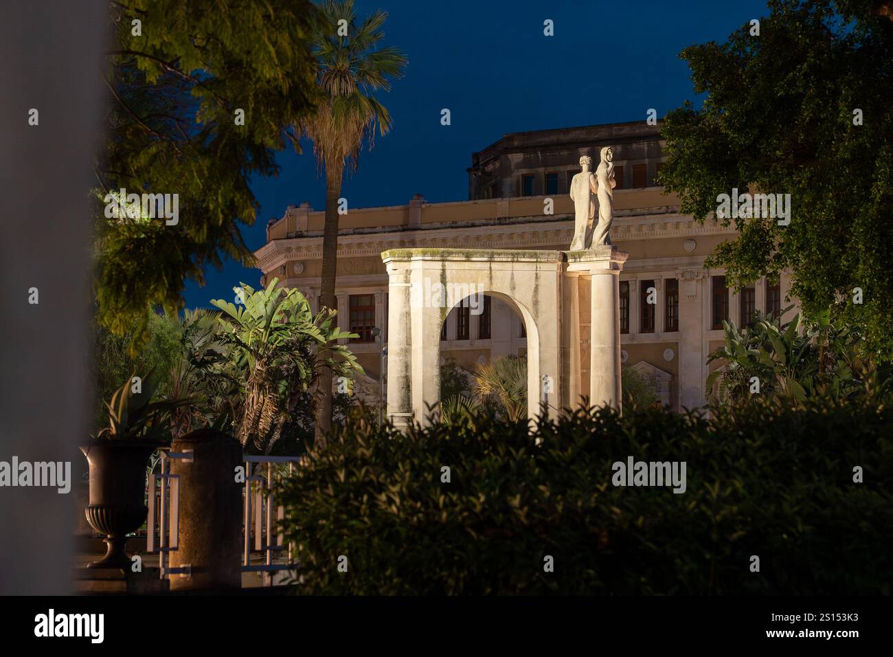 A beautifully lit stone arch adorned with statues in Giardino Bellini ...
