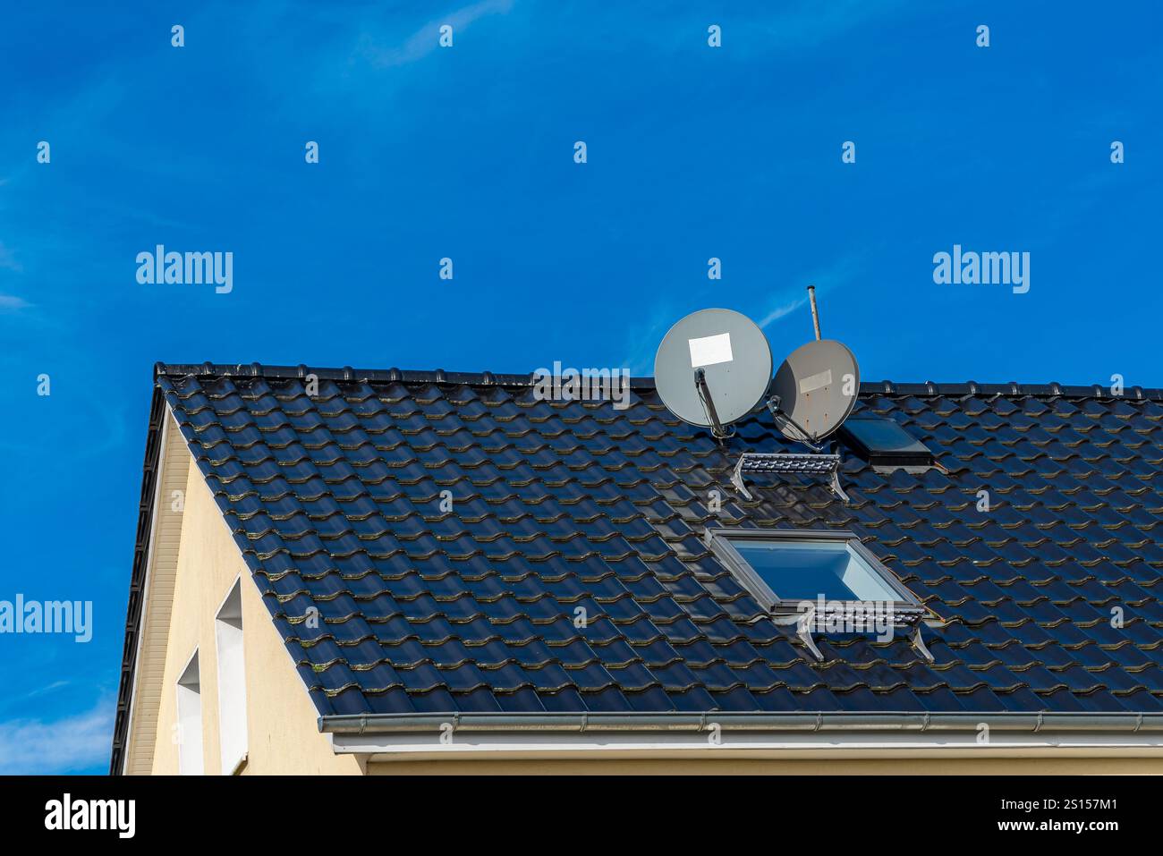 Two satellite dishes are installed on a sloped dark roof. A small ...