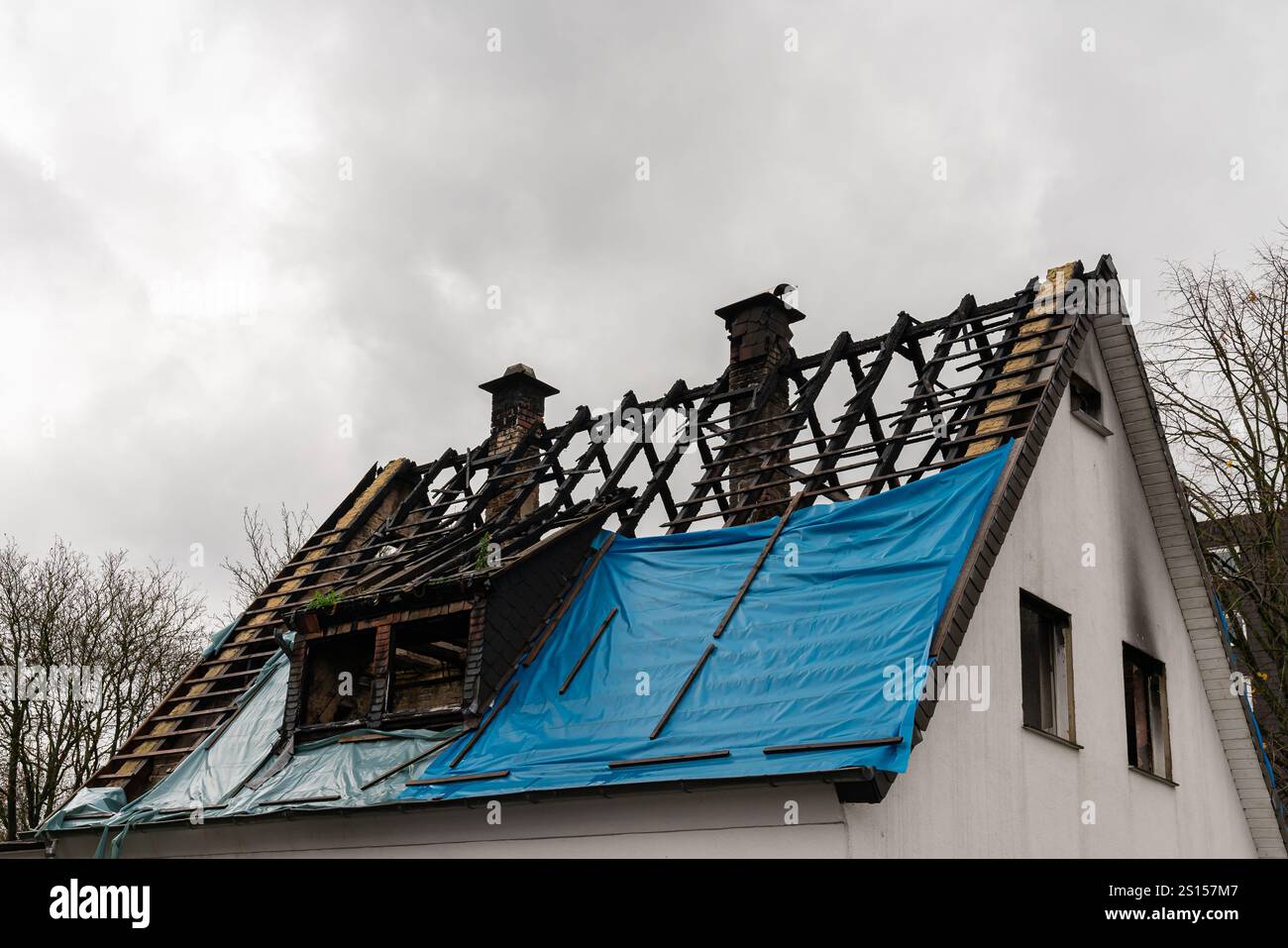 A house with significant fire damage on the roof shows charred beams ...