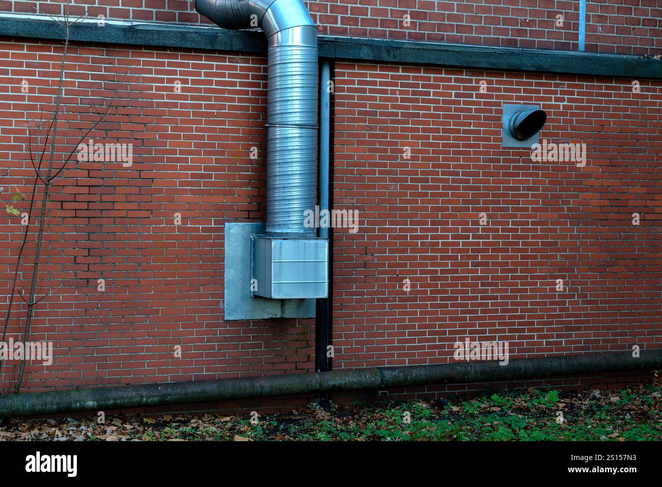 A metal ventilation duct extends from a brick wall, providing air ...