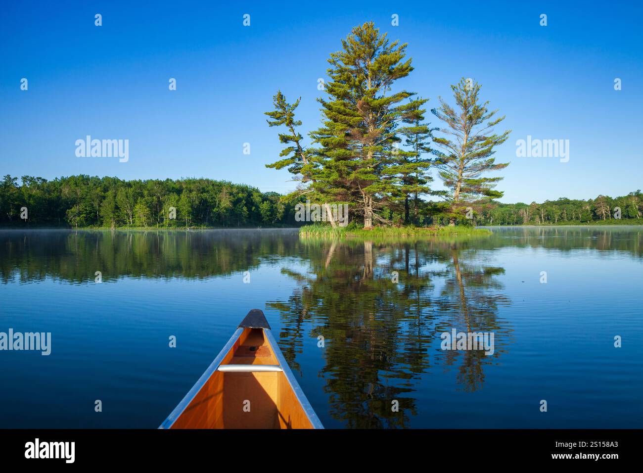 Front of a canoe on a beautiful calm blue lake with and island and pine ...
