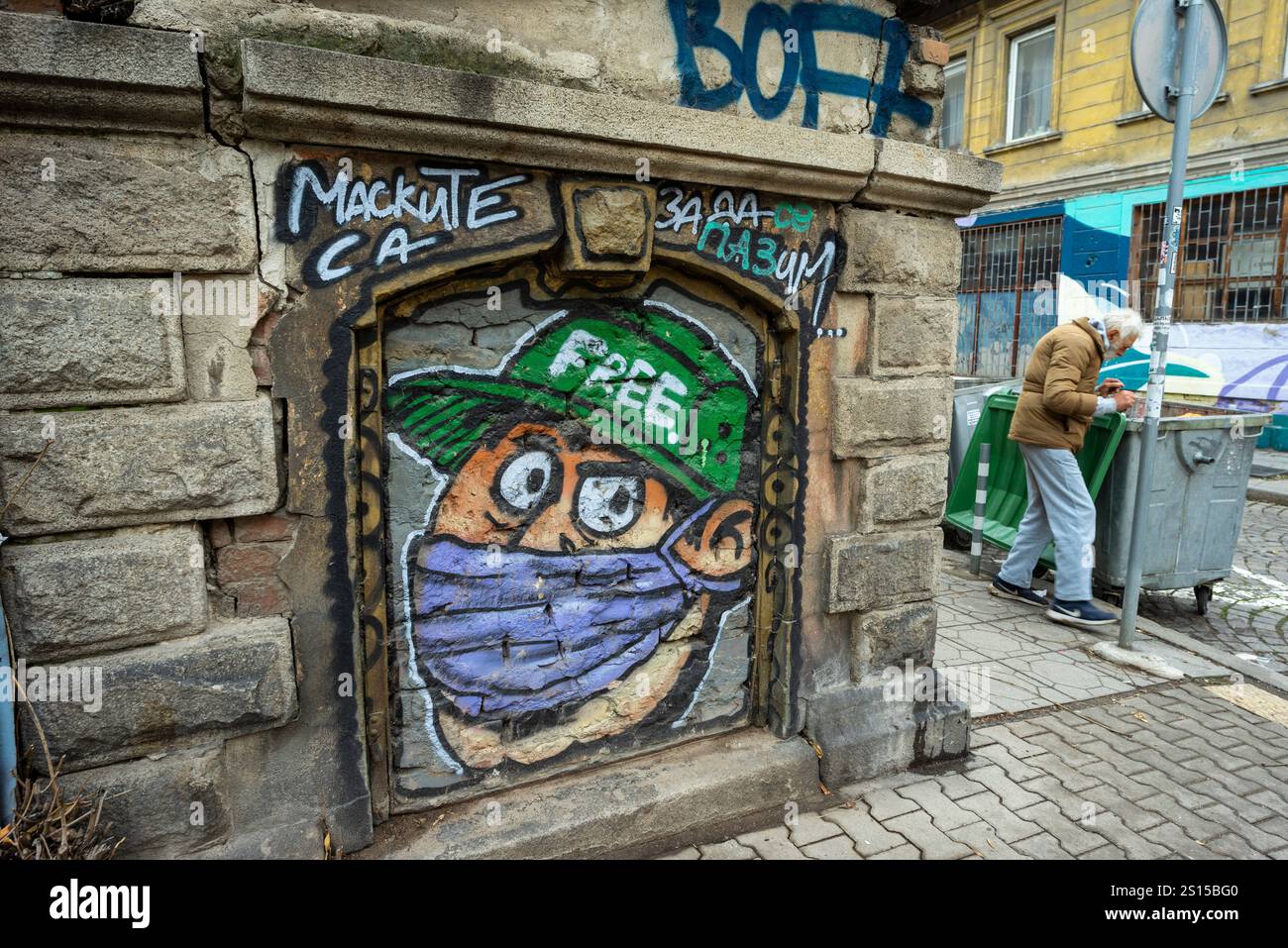 Homeless man rummaging through garbage next to graffiti calling for ...