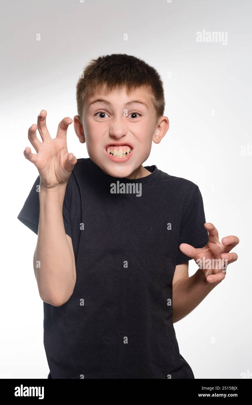 A young boy with a fierce expression, claws outstretched. He's wearing a dark shirt against a ...